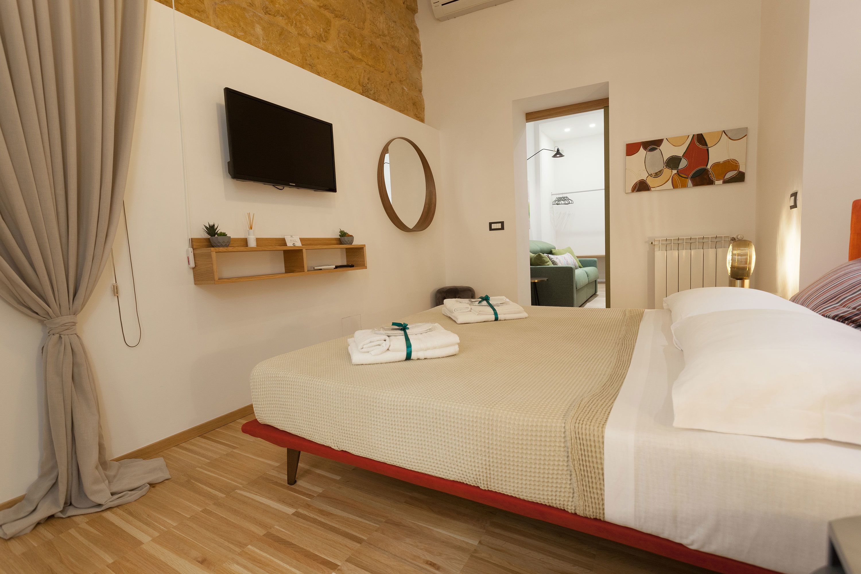 Quarto com cama, televisão, espelho e prateleira na parede com objetos decorativos.