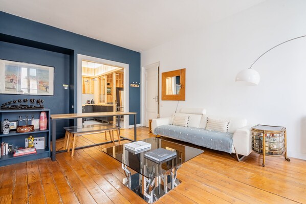 Uma sala de estar moderna com uma mesa de centro de vidro, um sofá branco e piso de madeira.