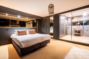 Quarto moderno com cama grande, box de vidro e banheiro à vista.