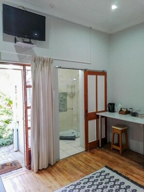Quarto com porta de vidro deslizante que dá para uma área de chuveiro, um banquinho de madeira e uma TV de tela plana fixada na parede.