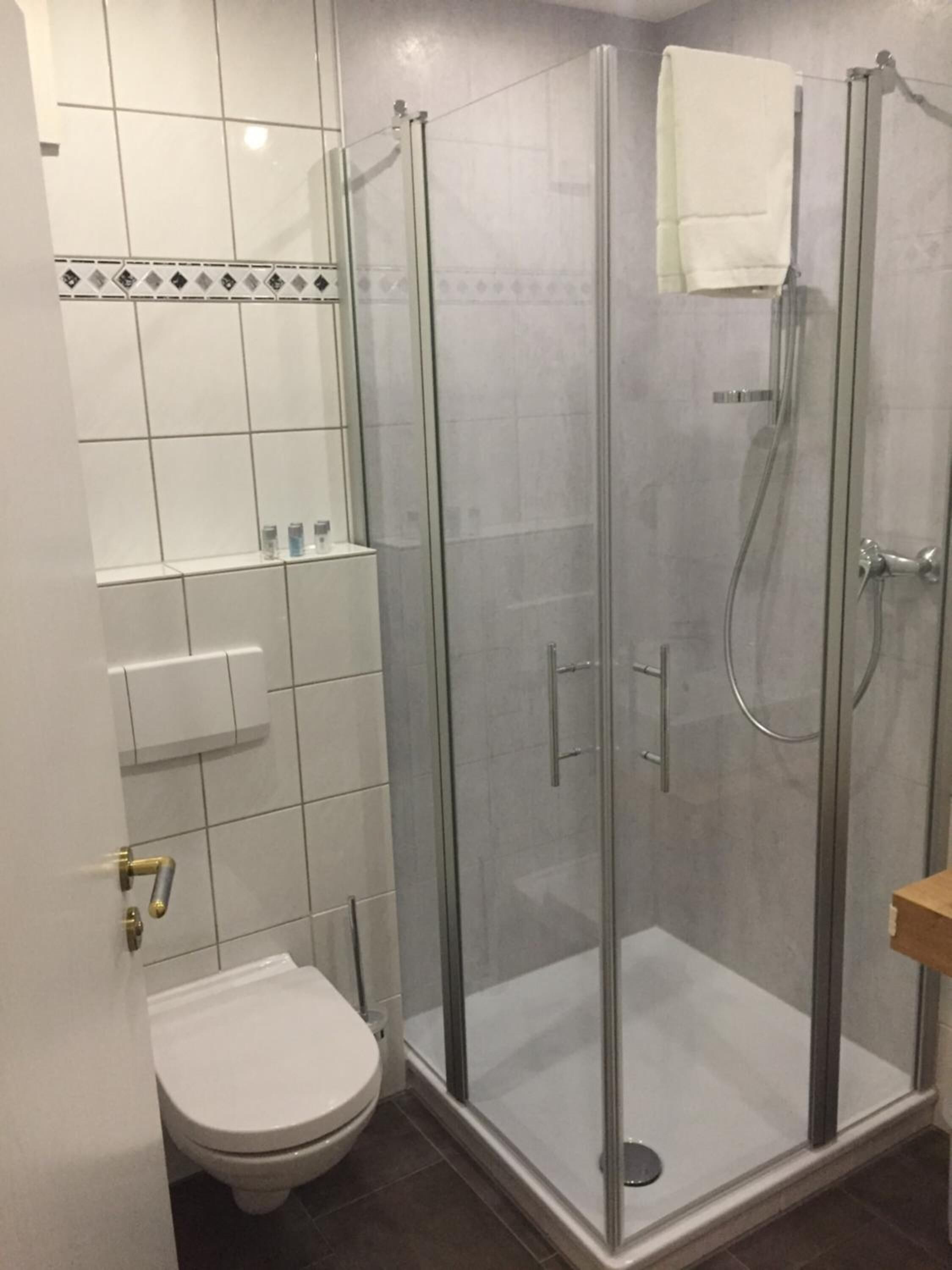 Uma casa de banho moderna com chuveiro em cabine de vidro, sanita e uma pequena prateleira com artigos de higiene pessoal.