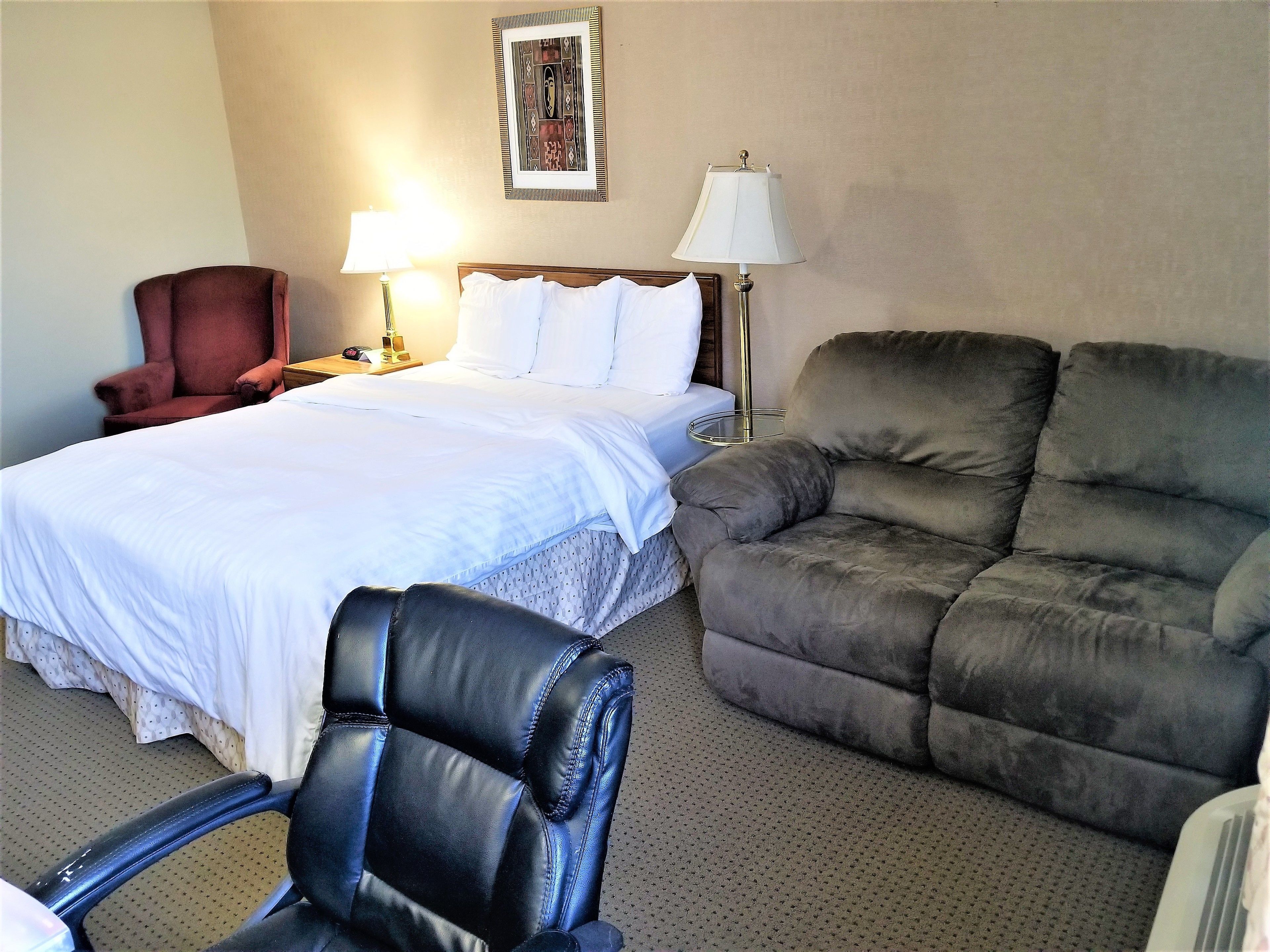 Quarto de hotel com uma cama, um sofá cinzento, um poltrona vermelha e uma cadeira de couro preto.