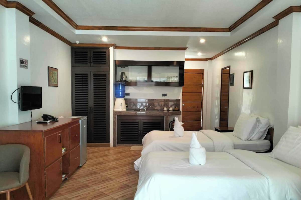 Quarto de hotel com cama, escrivaninha, cadeira, cozinha compacta e televisão.