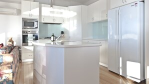 Uma cozinha moderna com armários brancos, uma ilha central, eletrodomésticos de aço inoxidável e uma geladeira grande.