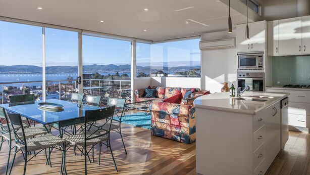 Uma cozinha moderna com uma ilha grande, uma área de refeições com mesa de vidro e um sofá.