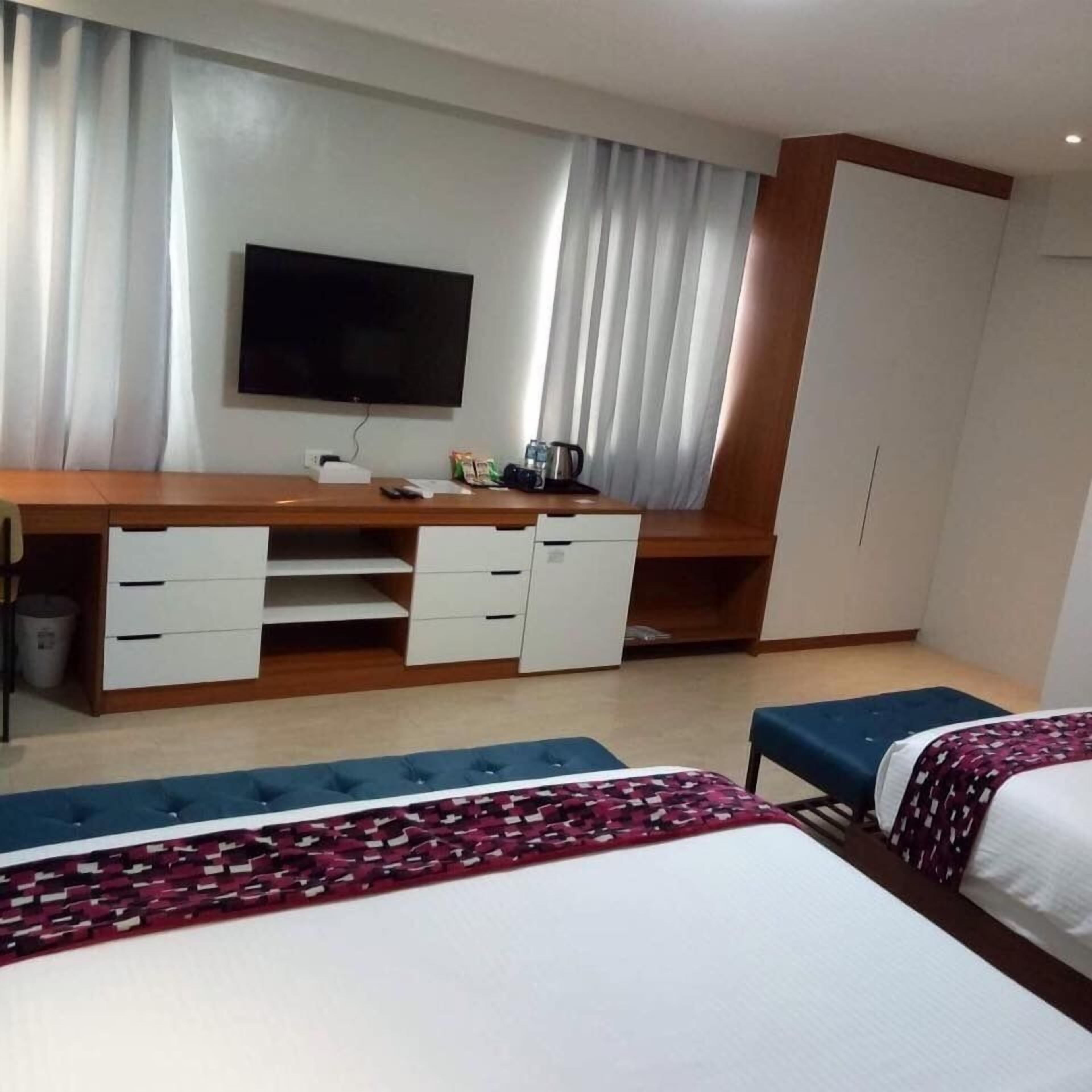 Quarto de hotel com cama, escrivaninha e televisão de tela plana, e um guarda-roupa.