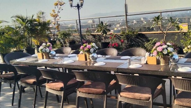 Uma área de refeições no terraço com mesas e cadeiras de vime, rodeada por plantas e flores em vasos.