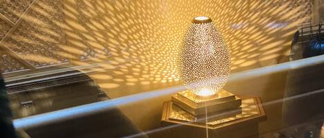 Luminária decorativa com padrões intrincados em um suporte, diante de um pano de fundo com desenhos ornamentais nas paredes.