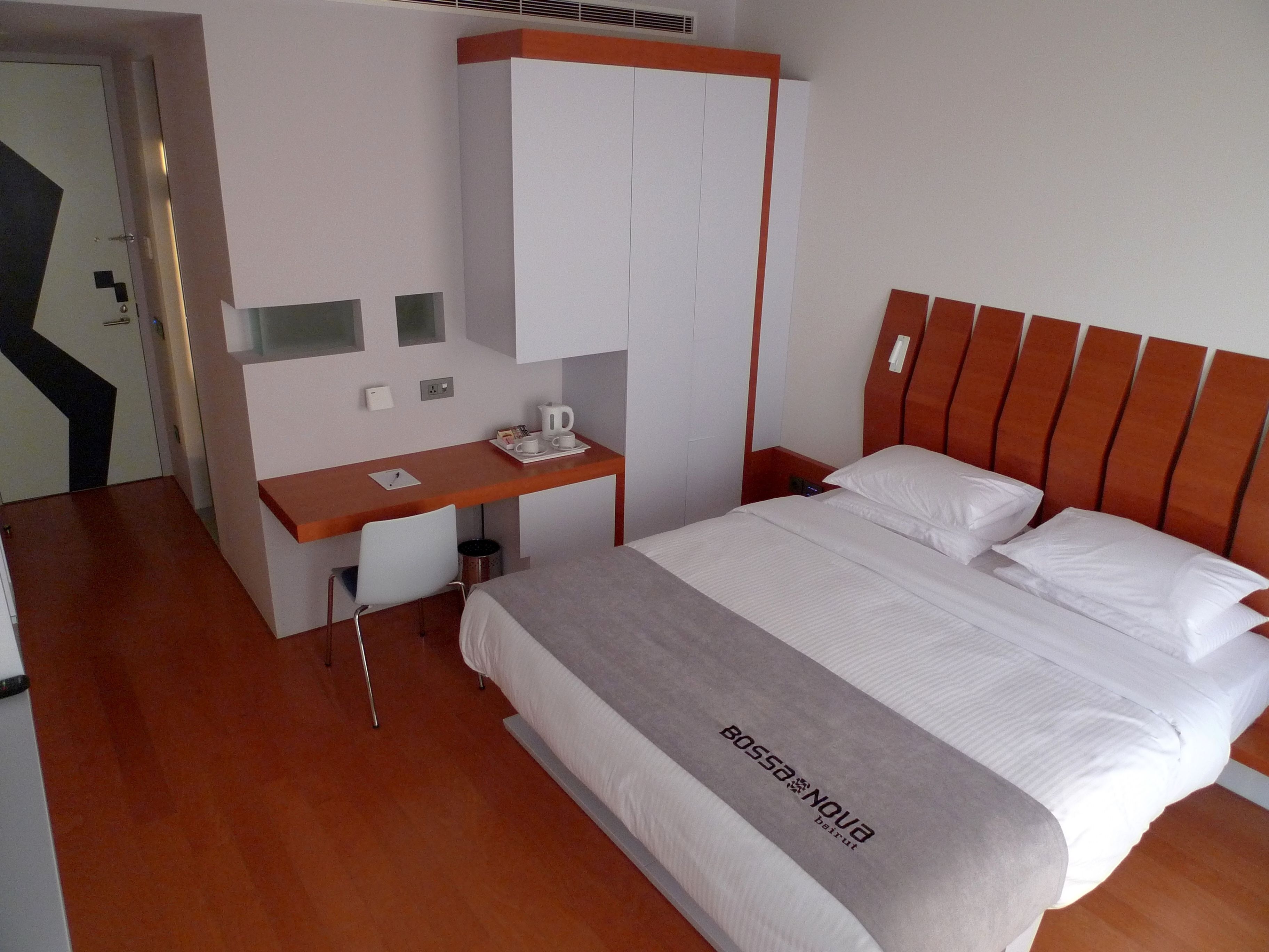 Quarto de hotel com uma cama, uma escrivaninha e um guarda-roupa.