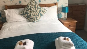 Cama bem arrumada com colcha verde-água, almofadas brancas e um padrão de papel de parede floral.