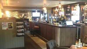 Uma área de bar com móveis de madeira, um balcão e uma parede de pedra.