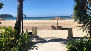 Uma praia com palmeiras, um guarda-sol de palha e cadeiras de praia.
