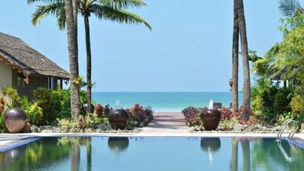Área de piscina com vista ampla para o oceano, cercada por palmeiras e plantas tropicais.