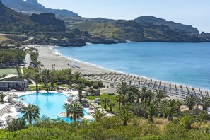 Na praia, espreguiçadeiras, guarda-sóis, prática de vôlei de praia 