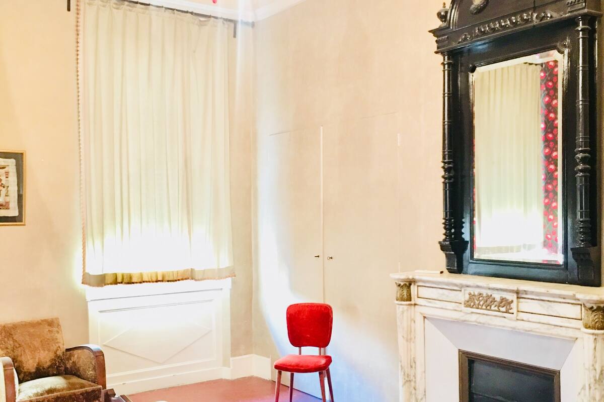 Um quarto com cama, uma cadeira vermelha, lareira e um candelabro.