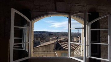 Quarto com janela em arco que dá para um vale com edifícios em terraços.