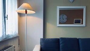 Quarto com sofá, luminária de chão, radiador e relógio na parede.
