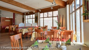 Restaurante com vigas de madeira, amplas janelas e mesas postas para refeições.