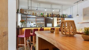 Uma área de bar com balcão de madeira, banquetas vermelhas e diversas garrafas e copos nas prateleiras.