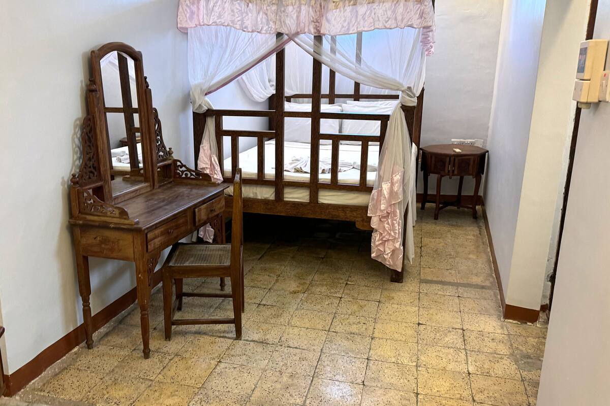 Um quarto com uma cama de madeira, uma escrivaninha de madeira, uma cadeira e uma pequena mesa de cabeceira.