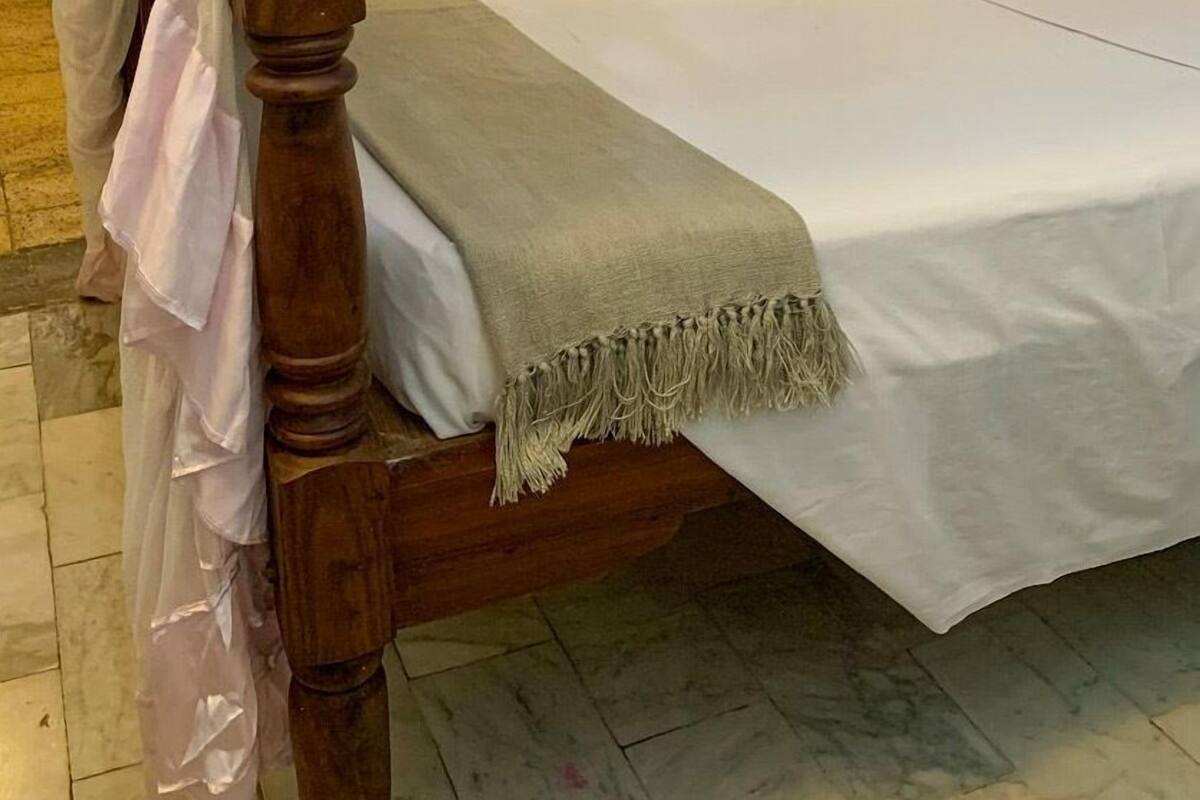 Uma cama de dossel com cortinas, roupa de cama branca e um cobertor bege.