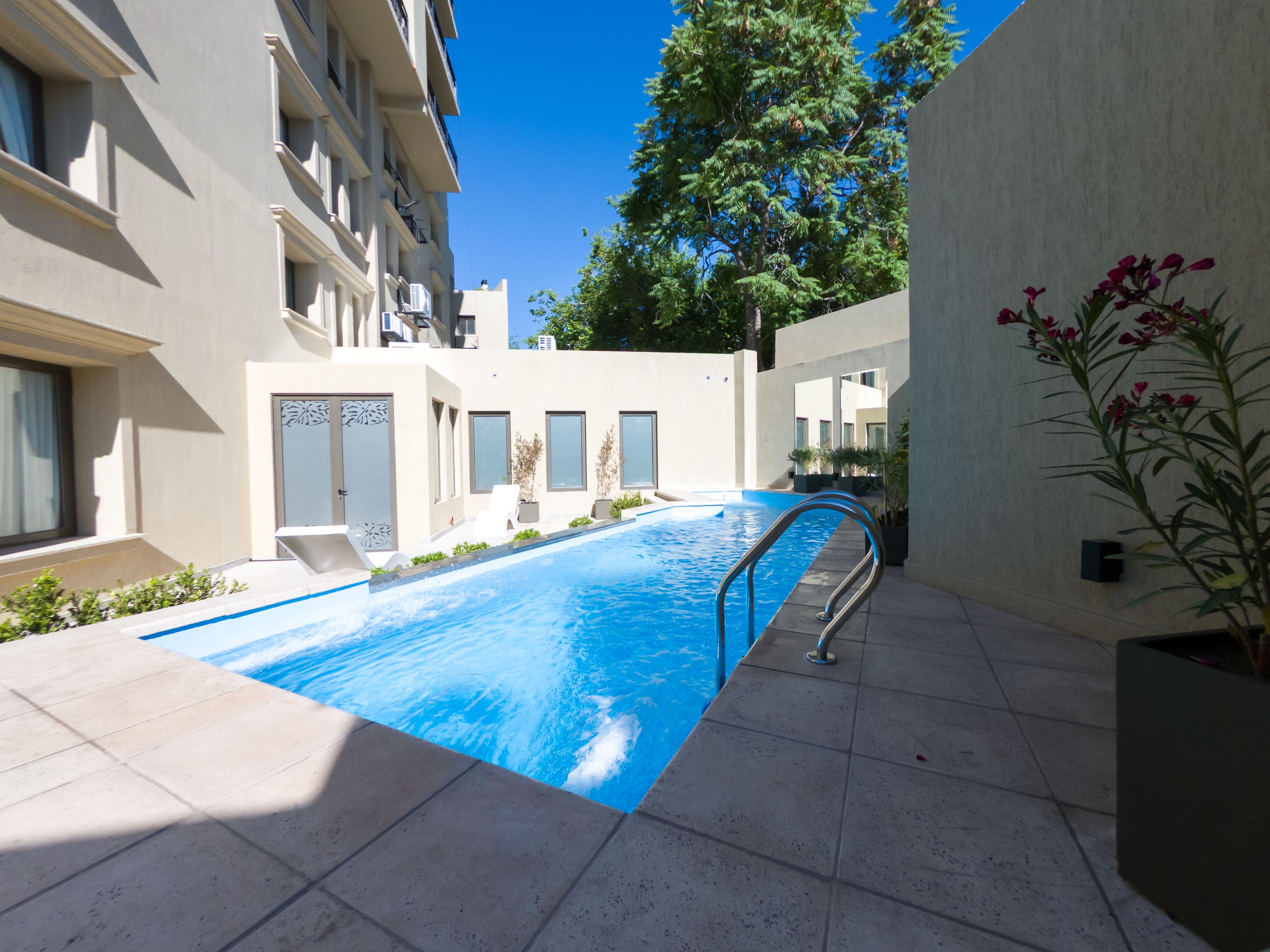 Piscina com escada de metal, cercada por um edifício com varandas e um vaso de planta.