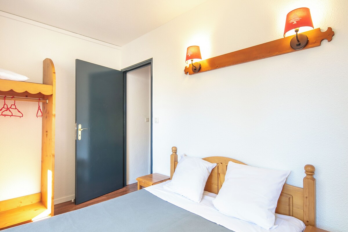 Quarto com cama, cabeceira de madeira, mesas de cabeceira, prateleira na parede com luminárias e uma porta.