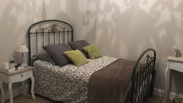Cama bem arrumada com colcha estampada, dois travesseiros, abajur e mesa de cabeceira com controle remoto e uma garrafa.