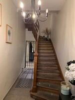 Uma escadaria de madeira com um lustre, um quadro emoldurado na parede e um vaso com flores no patamar.