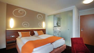 Quarto de hotel com uma cama grande, uma cadeira vermelha, uma mesa de cabeceira de madeira e um espelho sobre a cômoda.