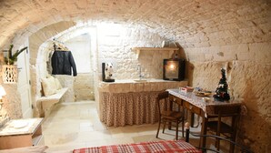 Um quarto acolhedor com um arco de pedra, uma pequena cozinha, uma mesa de jantar e uma cama com colcha xadrez.