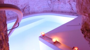 Quarto com paredes de pedra, uma banheira branca e duas velas sobre um parapeito.