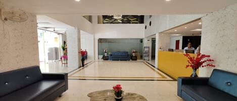 Um hall amplo com uma mesa de recepção, dois sofás, uma mesa de centro com flores e um sofá azul.
