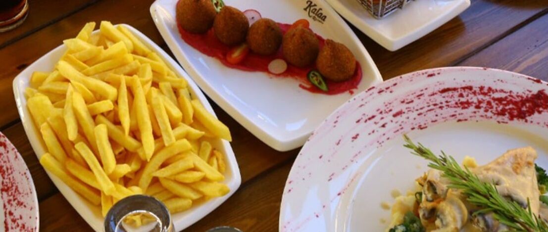 Uma mesa com um prato de batatas fritas, um prato com almôndegas ao molho e um prato com peixe.