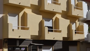 Um edifício de vários andares com varandas, uma garagem e um carro estacionado na frente.