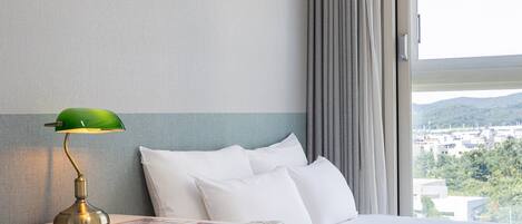 Quarto de hotel com duas camas, mesa de cabeceira com abajur, janela com cortinas e vista para a cidade.