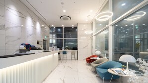 Um hall de hotel moderno, com piso de mármore, balcão de recepção, área de estar com sofás e grandes janelas.