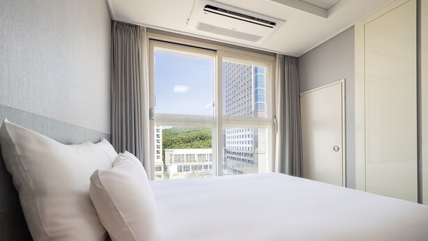 Quarto de hotel moderno com uma cama grande, vista da cidade e cortinas.