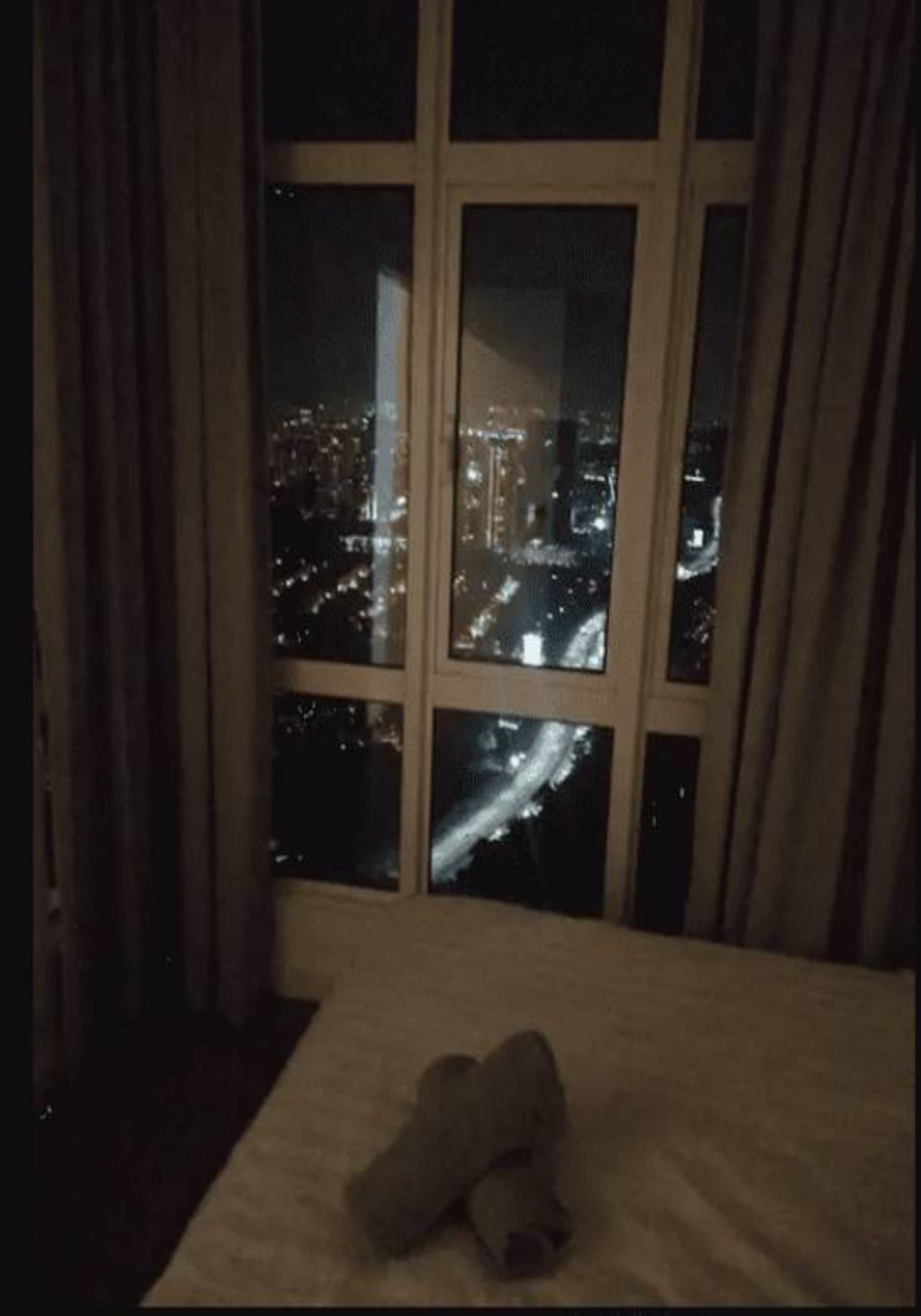 Quarto com uma grande janela com vista para a paisagem urbana à noite.