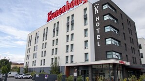 Um hotel moderno com uma placa vermelha grande, vários andares e fachadas de tijolos brancos e escuros.