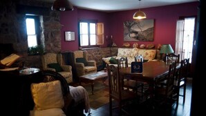 Uma sala de estar acolhedora com parede de pedra, um sofá, poltronas, uma mesa de jantar e um quadro na parede.