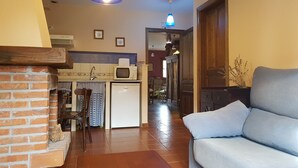 Uma sala de estar com sofá, lareira de tijolos, cozinha com micro-ondas e área de jantar com cadeiras.