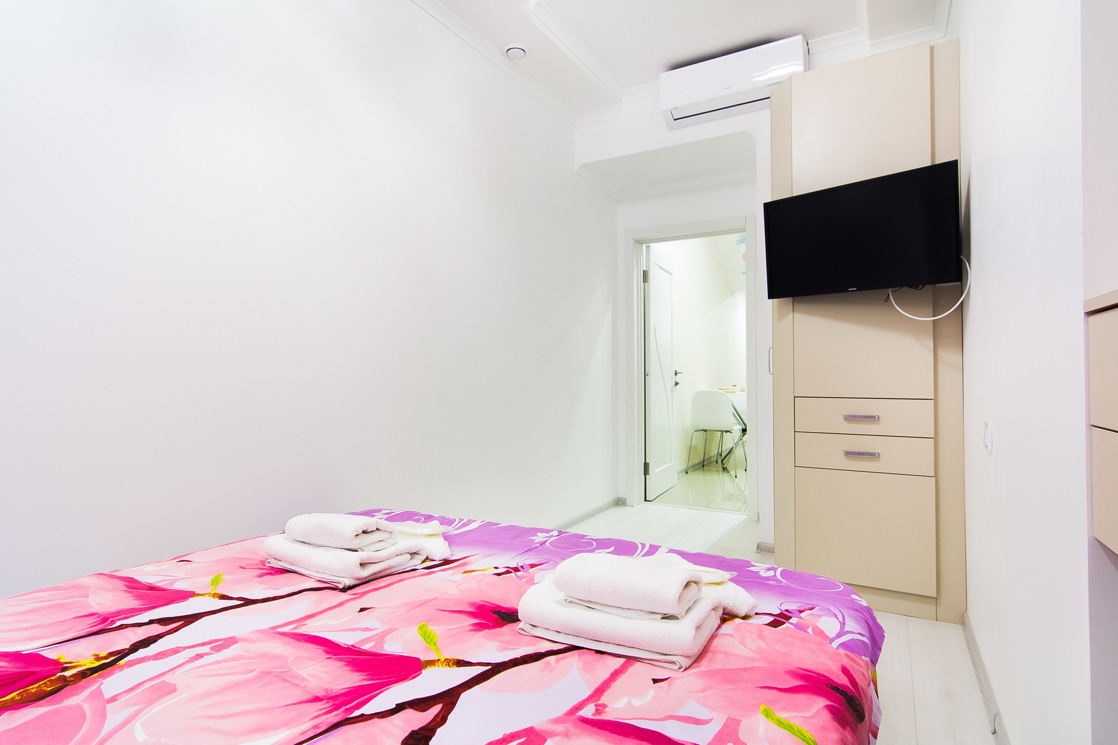 Quarto com cama, televisão presa na parede e guarda-roupa.
