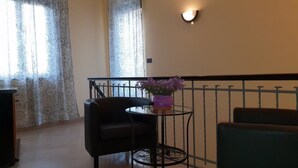 Quarto com uma poltrona de couro preto, uma mesinha redonda com um vaso roxo e um corrimão de varanda.