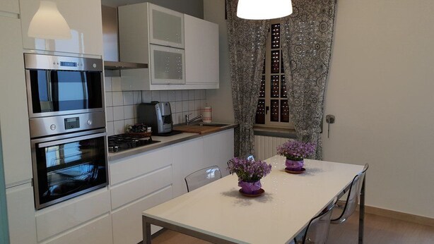 Uma cozinha moderna com eletrodomésticos embutidos, uma mesa de jantar com cadeiras e flores roxas decorativas.