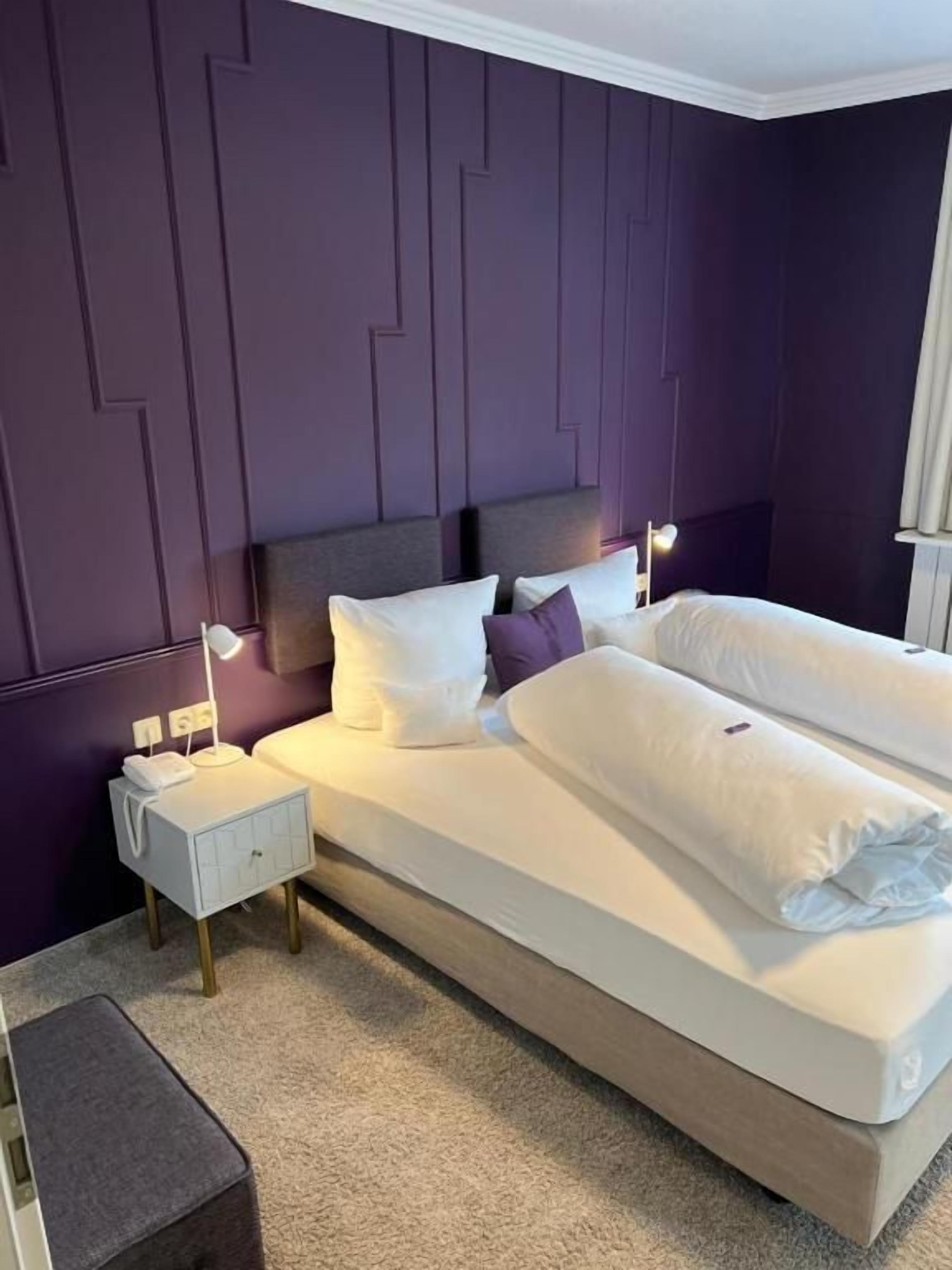 Quarto de hotel com uma cama grande, uma mesa de cabeceira e um criado-mudo.