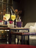 Uma área de bar com vários copos de bebidas, um pequeno vaso com flores secas e uma cadeira.