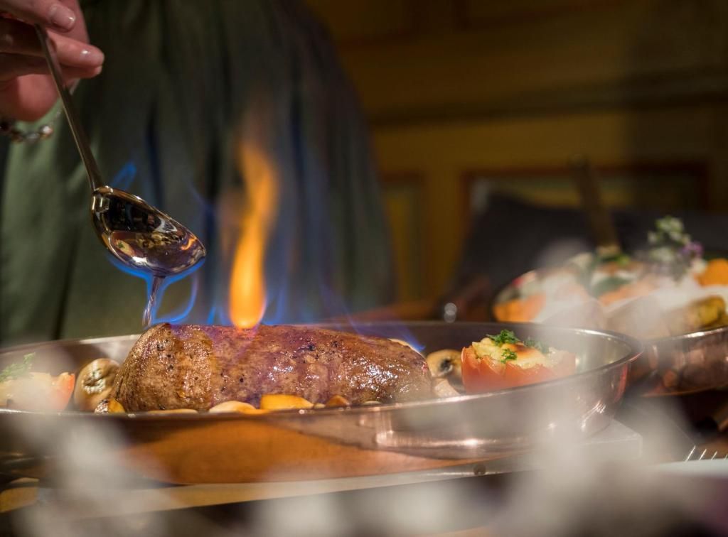 Pessoa cozinhando um bife na grelha com legumes e uma frigideira sobre uma mesa.