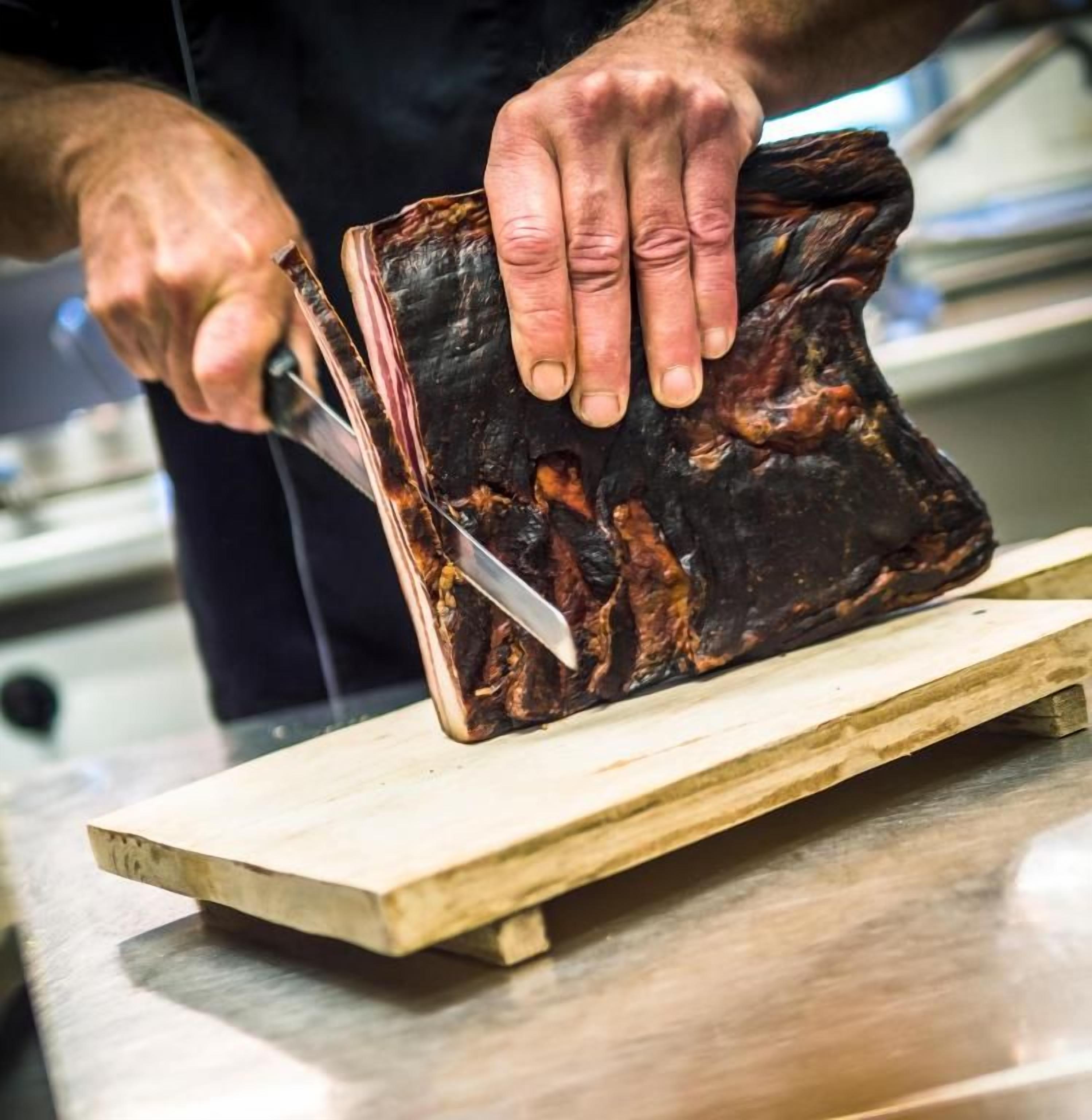 Uma pessoa cortando um pedaço grande de carne em uma tábua de madeira.