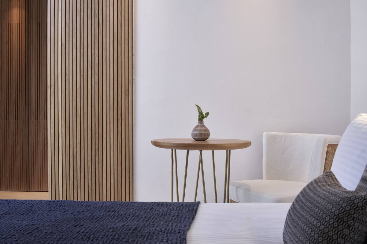 Um quarto moderno com uma cama, uma mesinha redonda com um vaso e uma cadeira.